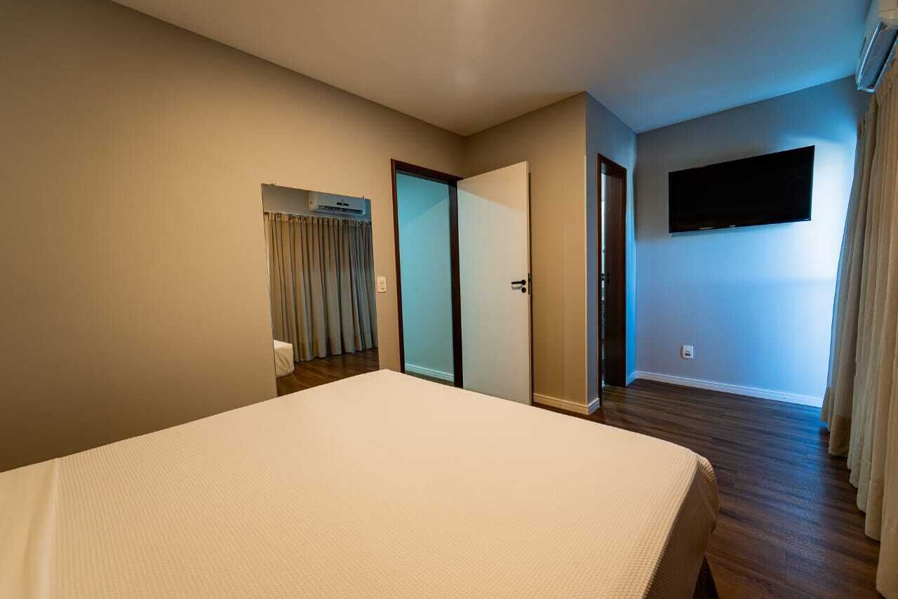 Quarto de hotel com uma cama, televisão presa à parede e porta que dá para outro quarto.