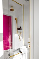 Um banheiro com vaso sanitário branco, porta rosa e chuveiro com detalhes dourados.