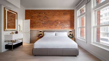 Quarto moderno com parede de tijolos em destaque, uma cama grande, um espelho sobre a penteadeira e mesas de cabeceira com abajures.