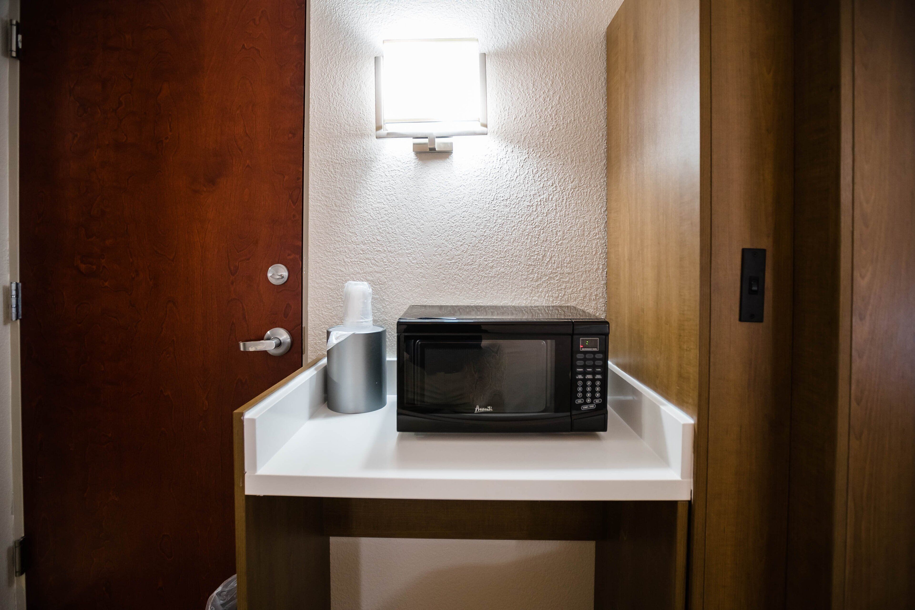 Um microondas sobre uma bancada branca em um quarto com porta de madeira e parede texturizada.