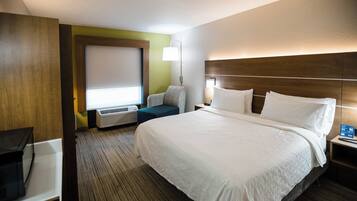 Quarto de hotel com uma cama grande, uma mesa de escritório, uma cadeira, mesa de cabeceira, abajur e janela com vista.