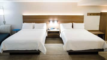 Quarto de hotel com duas camas, uma mesa de cabeceira, um abajur e iluminação embutida na parede.