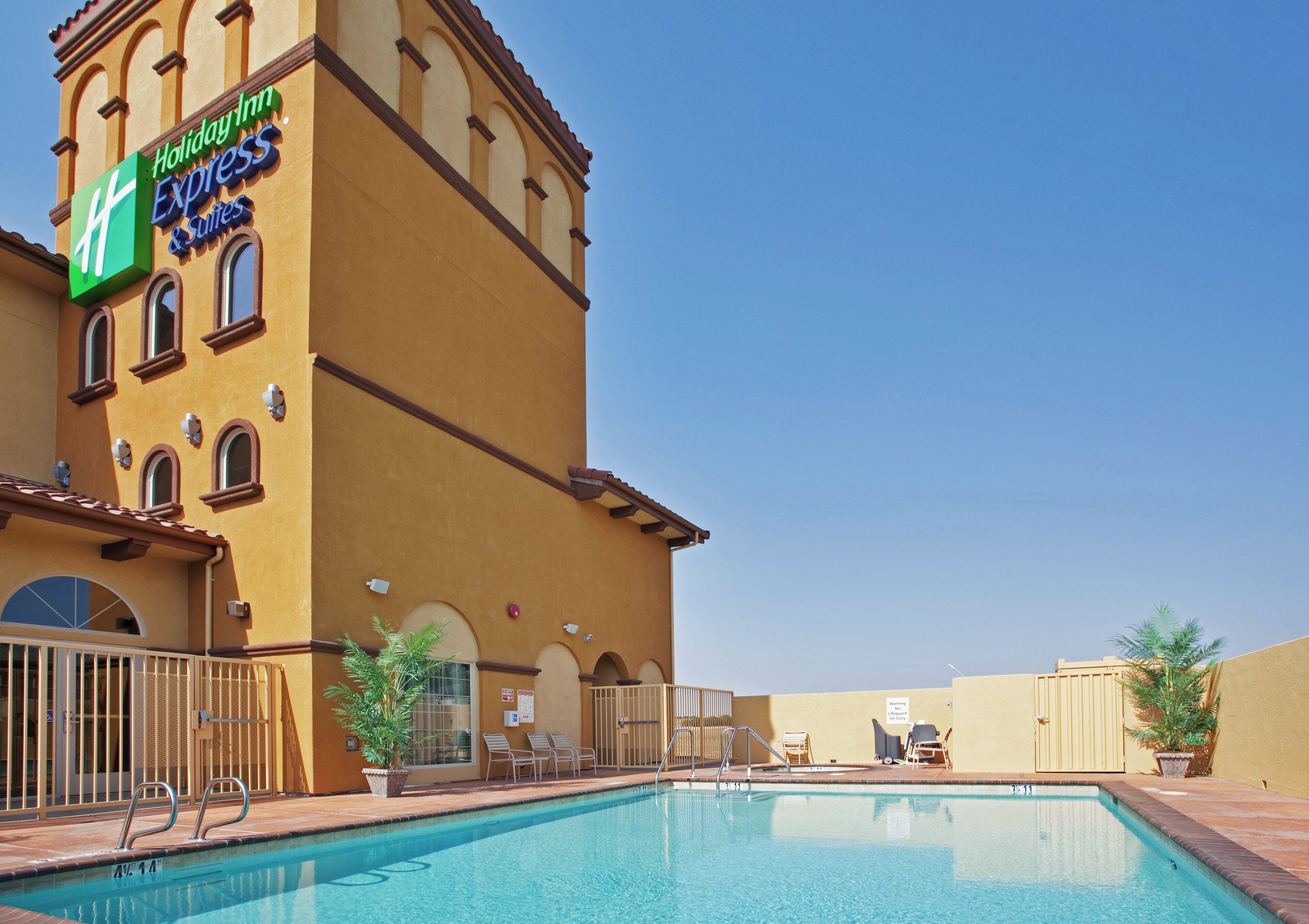 Edifício Holiday Inn Express Suites com piscina, área de estar externa e céu azul límpido.