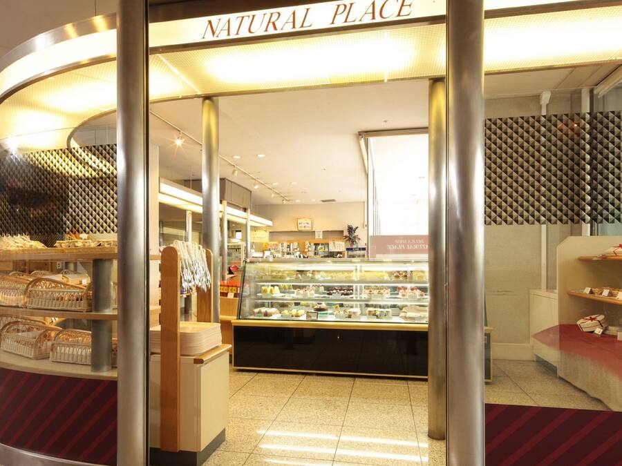 Uma padaria com uma vitrine repleta de doces e um letreiro com a inscrição "NATURAL PLACE".