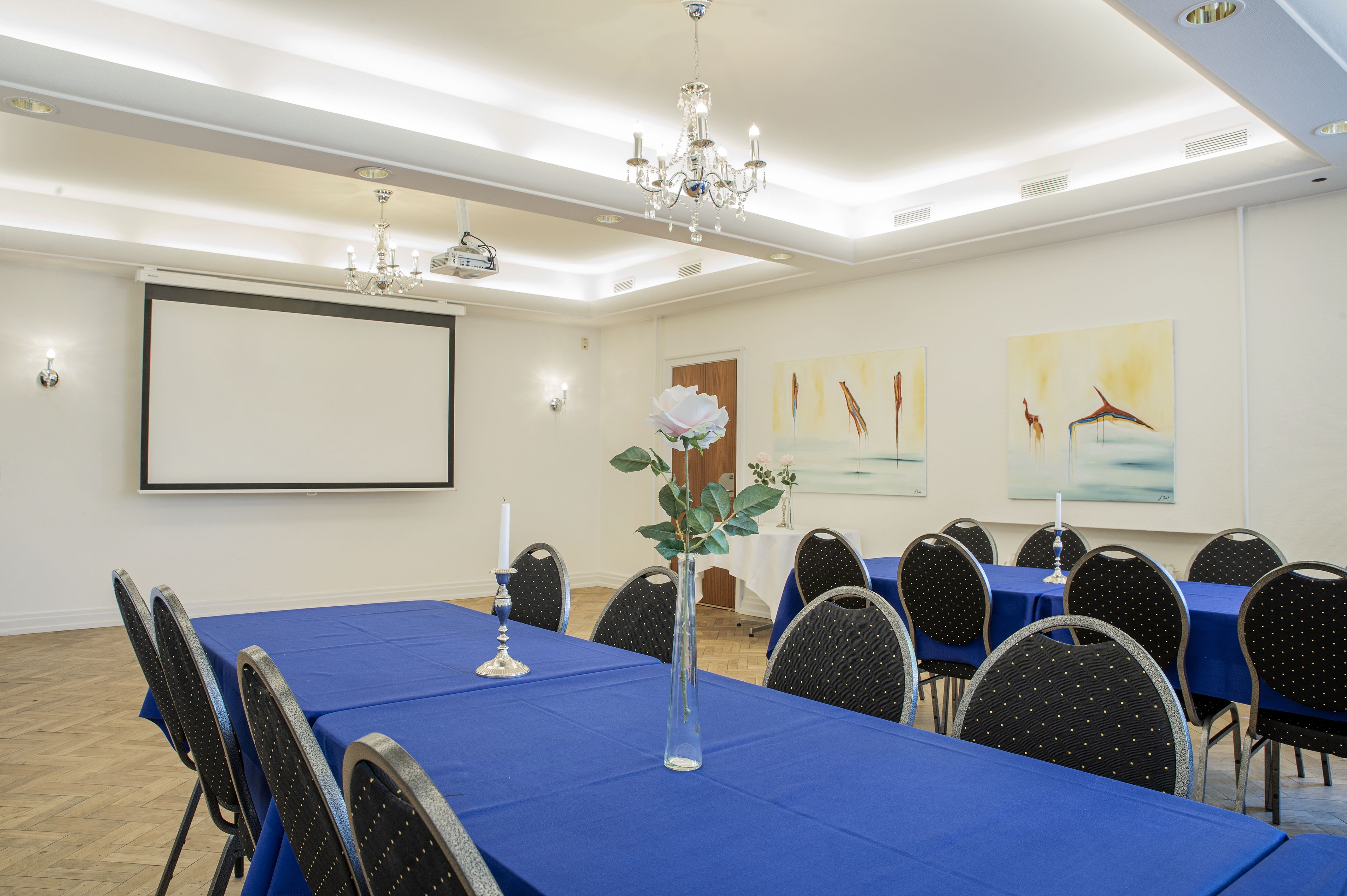 Uma sala de conferências com uma grande mesa, cadeiras, uma tela de projetor e obras de arte nas paredes.