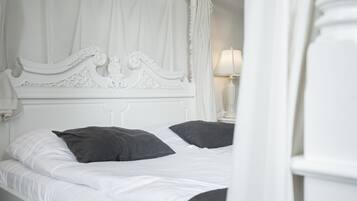 Uma cama branca com dossel, dois travesseiros e uma mesa de cabeceira com abajur.