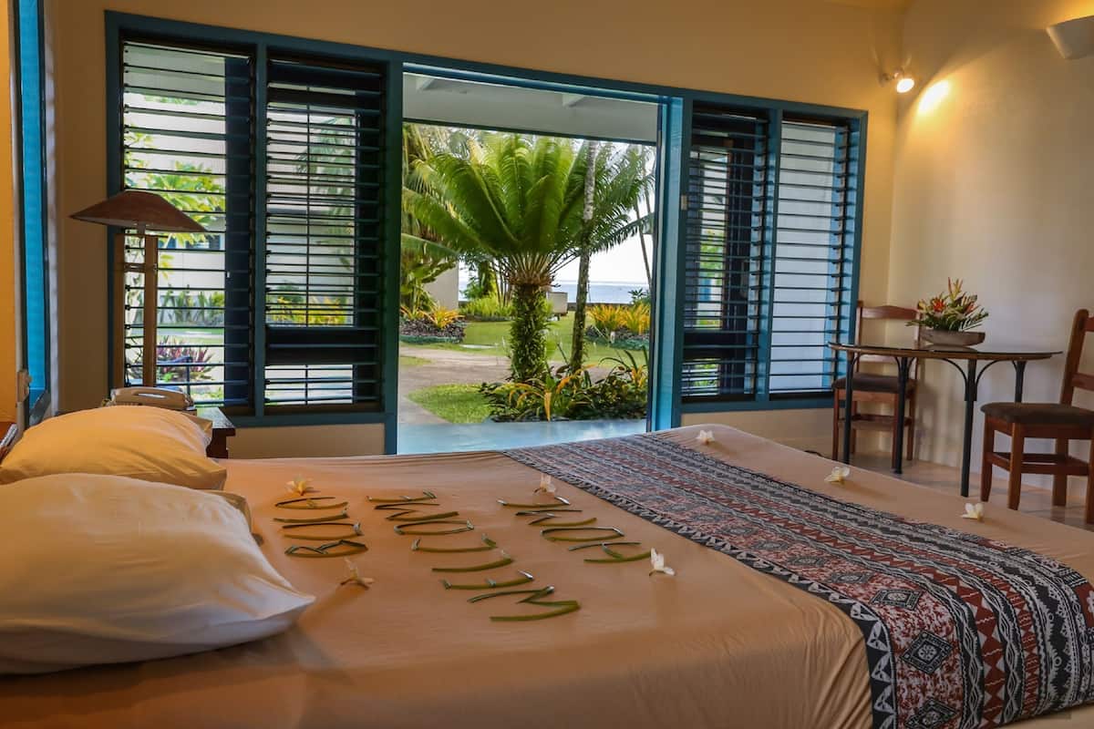 Quarto com cama, escrivaninha e vista para um jardim através de janelas abertas.