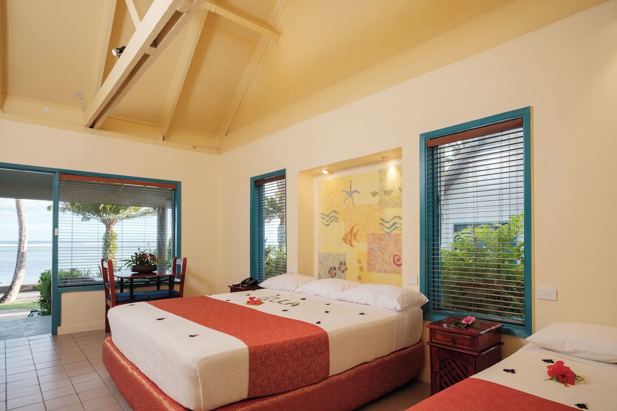 Quarto com cama, escrivaninha e cadeira, janela com persianas e vista para o mar.