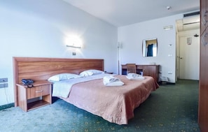 Quarto de hotel com cama, mesa de cabeceira, luminária e escrivaninha com cadeira.