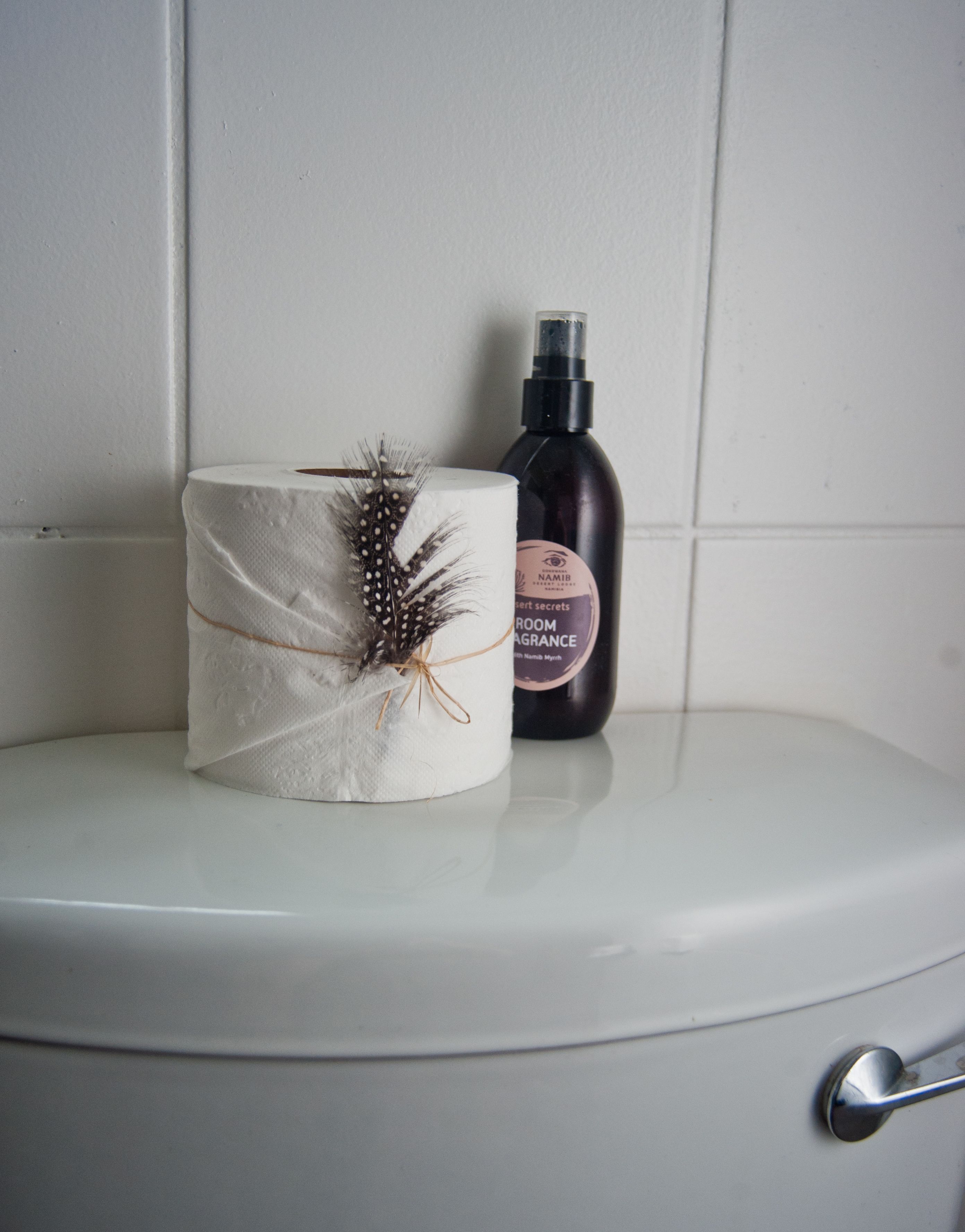 Sanitário com rolo de papel higiênico e um frasco de aromatizador em uma parede com azulejos brancos.