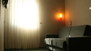 Quarto com sofá, televisão na parede, luminária e janela com cortinas.