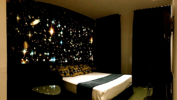 Quarto de hotel moderno com uma cama grande, uma mesa de cabeceira e uma parede com iluminação em formato de estrelas.