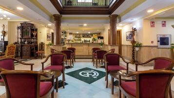 Um hall de hotel com área de bar, cadeiras estofadas em vermelho e uma fonte decorativa.