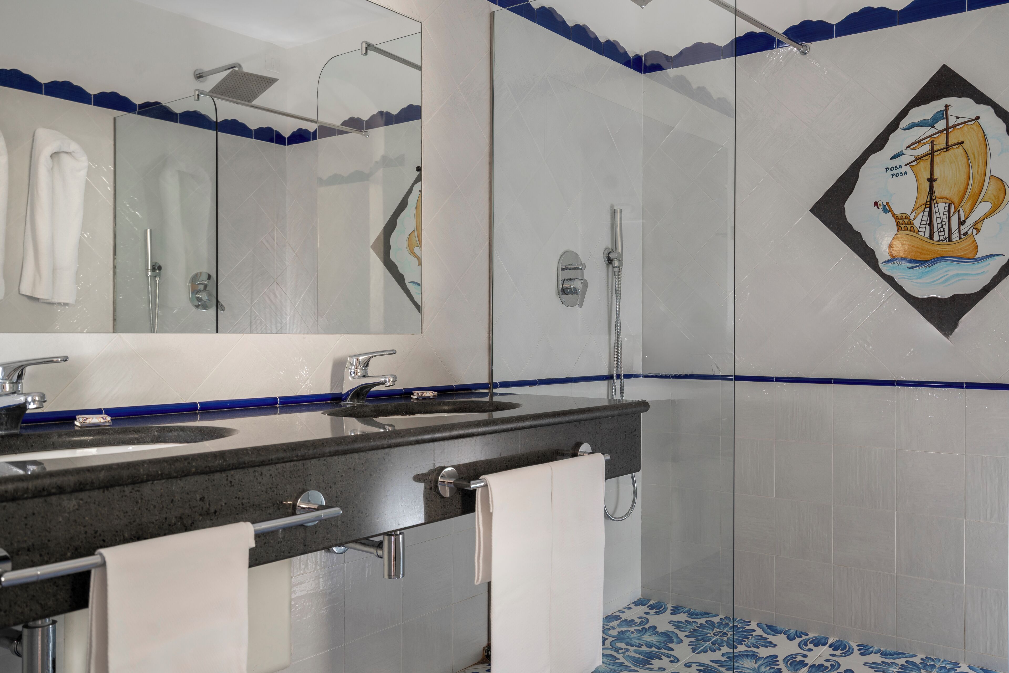 Casa de banho com duas pias, chuveiro e um mural decorativo de azulejos.