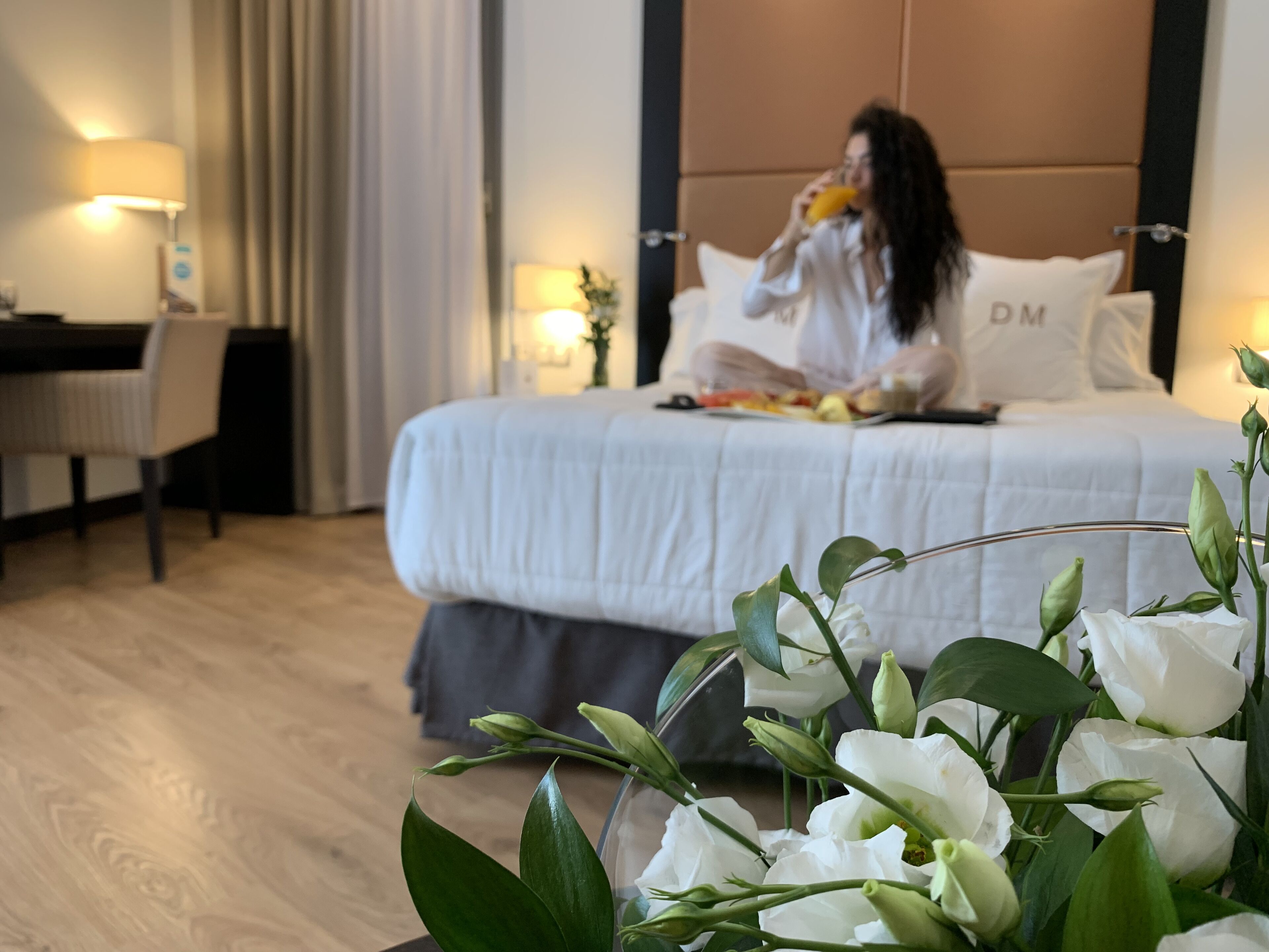 Quarto de hotel com cama, escrivaninha e cadeira. Arranjo de flores em primeiro plano.