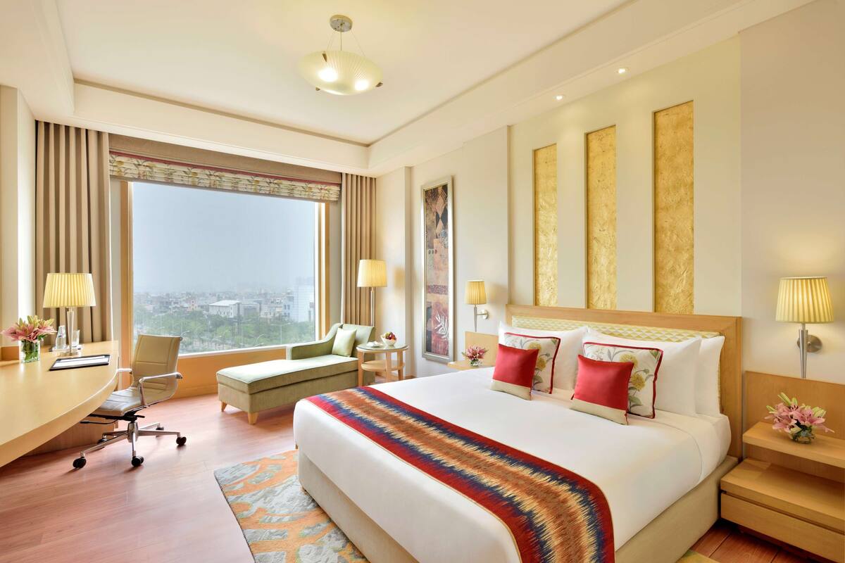 Quarto de hotel com cama grande, escrivaninha, cadeira e vista para a cidade.