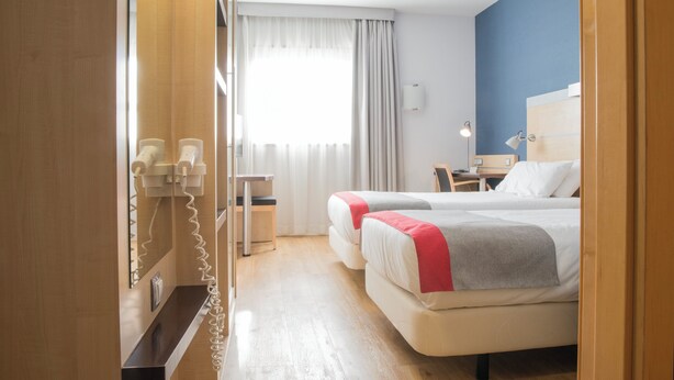 Quarto de hotel com duas camas, uma escrivaninha, uma cadeira e um telefone.