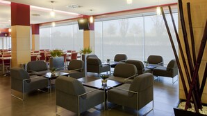 Uma sala de jantar moderna com mesas, cadeiras, janelas amplas e plantas decorativas.