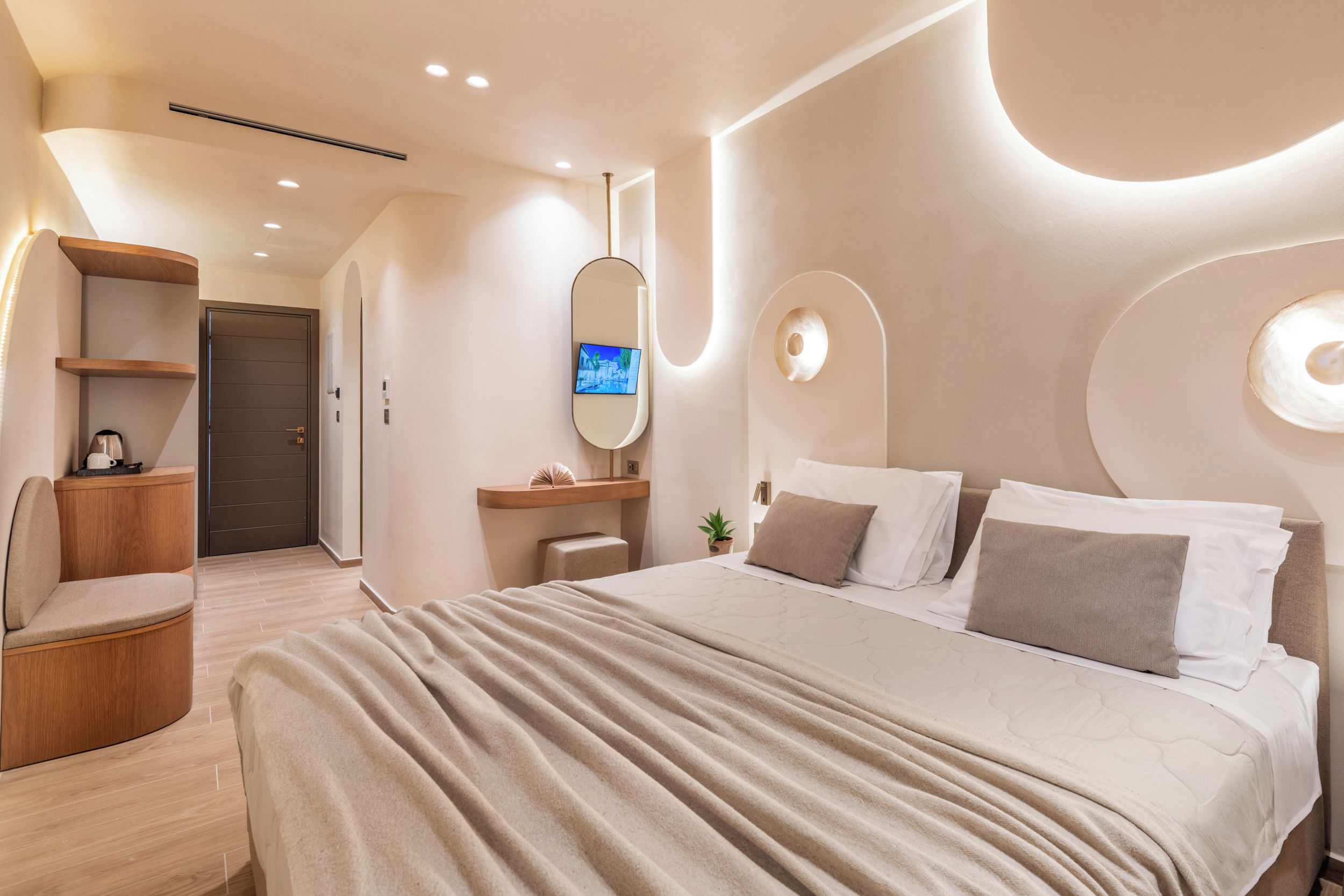 Quarto de hotel moderno com uma cama grande, uma cadeira de madeira, uma mesa pequena e uma TV fixada na parede.