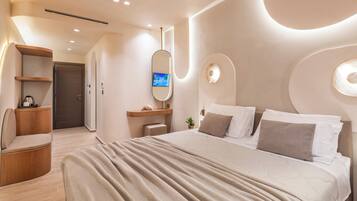 Quarto de hotel moderno com uma cama grande, uma cadeira de madeira, uma mesa pequena e uma TV fixada na parede.