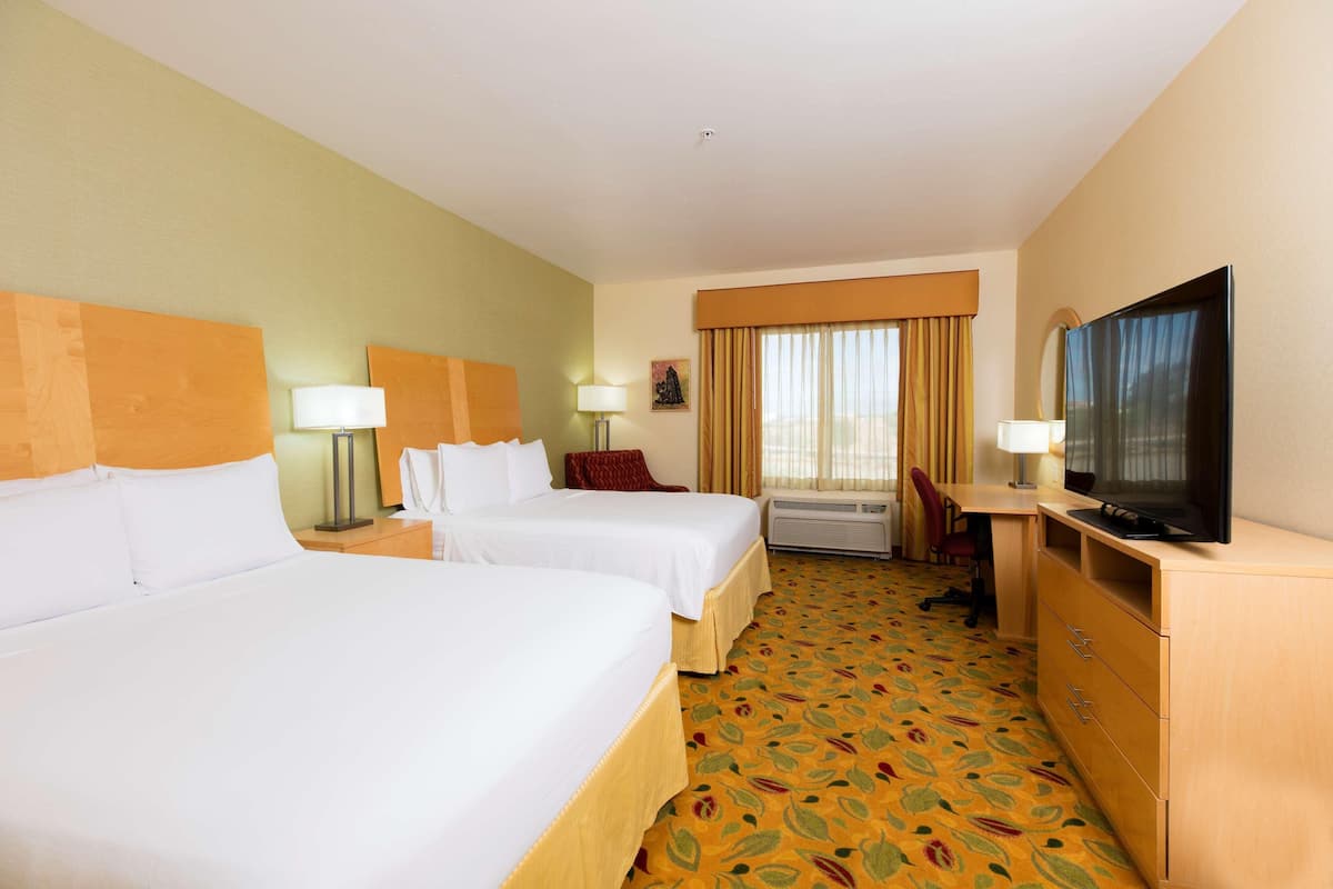 Quarto de hotel com duas camas, uma escrivaninha, uma televisão e um aparelho de ar condicionado.