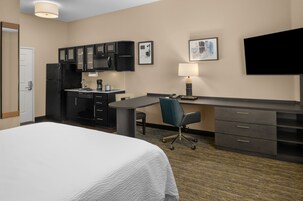 Quarto de hotel com cama, escrivaninha, cadeira, micro-ondas, geladeira, televisão e abajur.