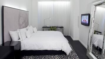 Quarto de hotel com uma cama grande, uma escrivaninha, uma cadeira, uma televisão e um espelho.