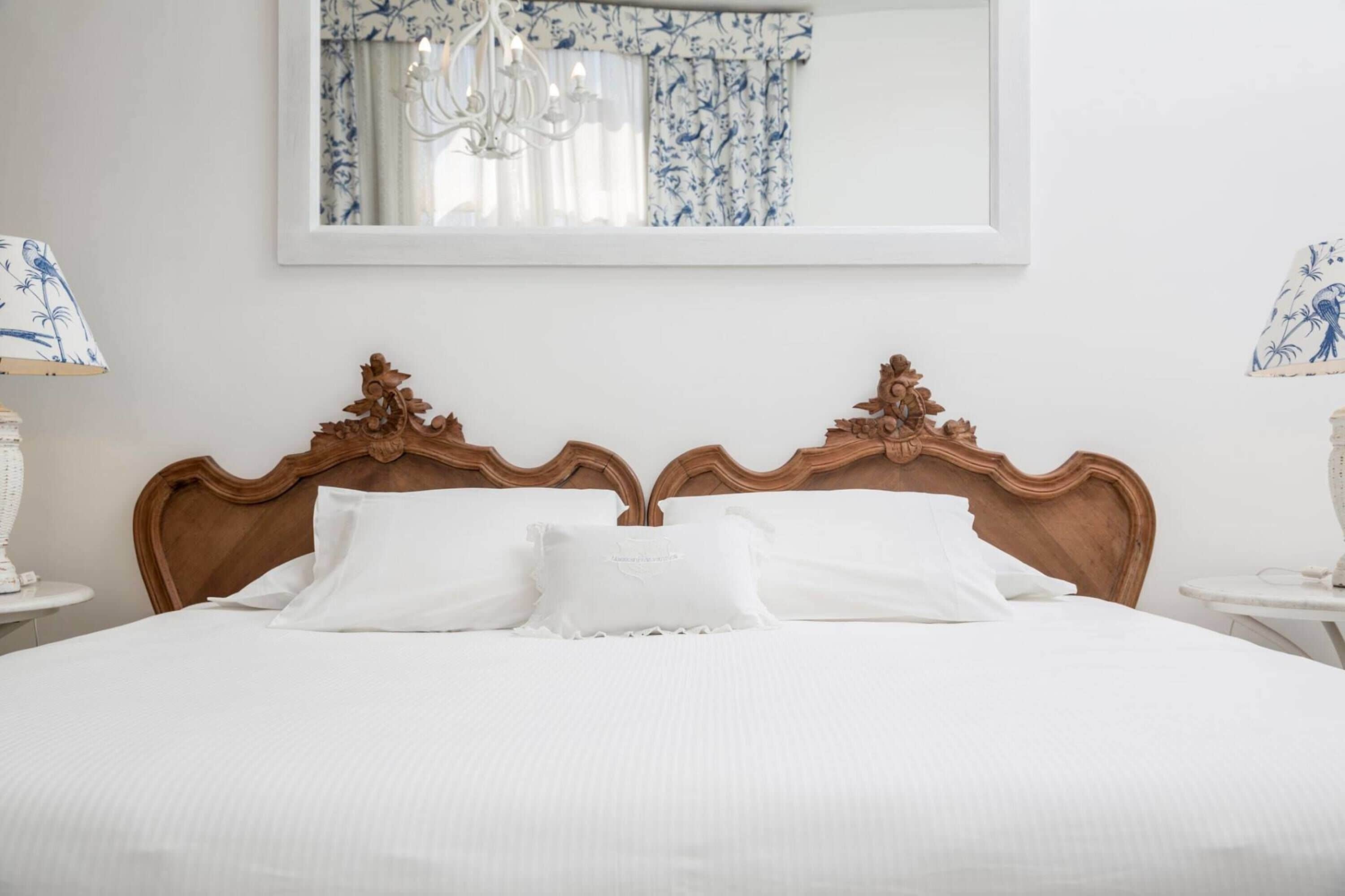 Uma cama bem arrumada com cabeceira de madeira, um espelho em cima e um candelabro ao fundo.
