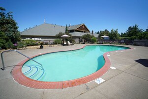 Piscina com borda de tijolos, mesa de piquenique e guarda-sol coberto.