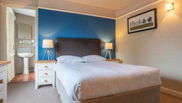 Quarto com uma cama grande, mesas de cabeceira, um criado-mudo, uma luminária na parede e um quadro emoldurado.