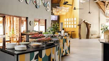 Disposição de buffet com diversos alimentos e pratos, um ventilador de teto e uma parede com decorações circulares.