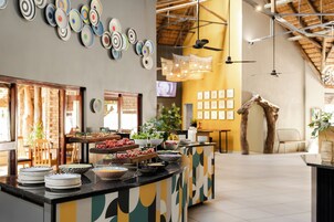 Disposição de buffet com diversos alimentos e pratos, um ventilador de teto e uma parede com decorações circulares.