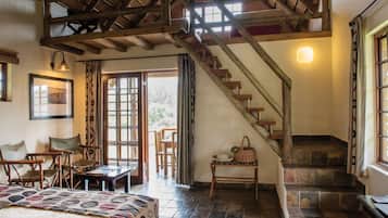 Um quarto rústico com escada de madeira, sala de jantar com cadeiras, mesa e cama com manta estampada.