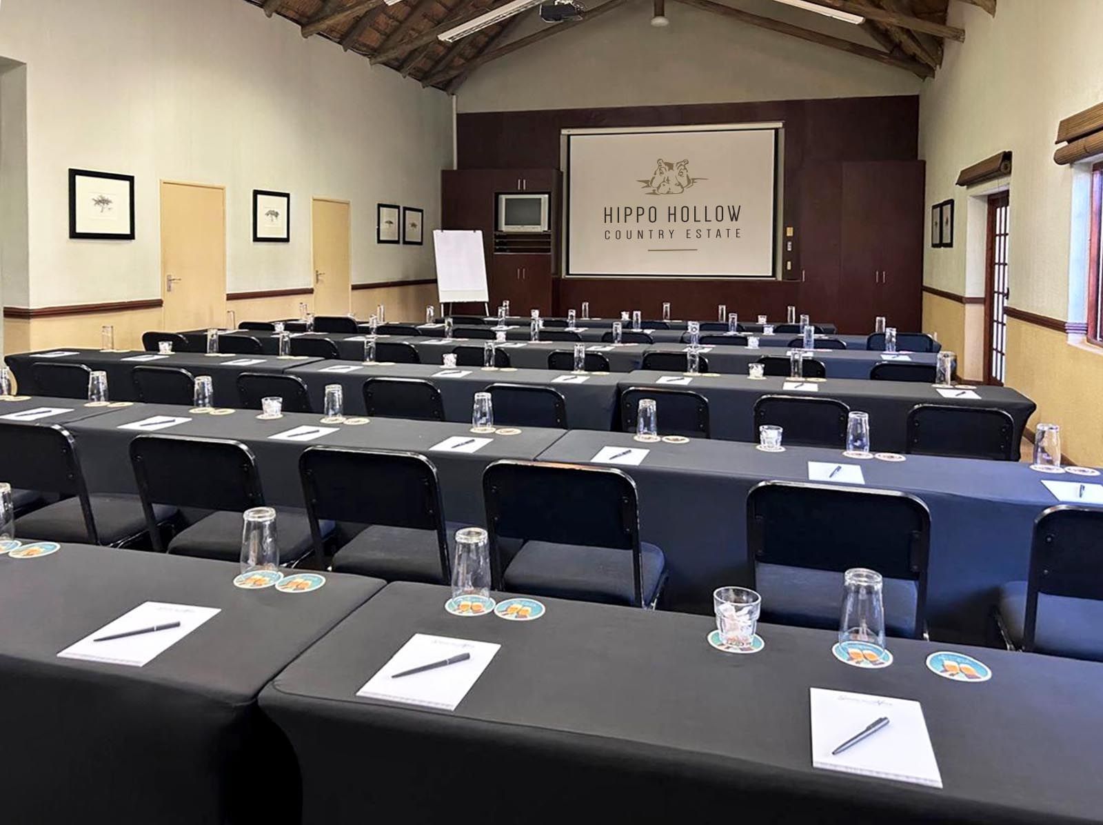 Uma sala de conferências com várias mesas, placas de identificação e uma tela exibindo 'HIPPO HOLLOW COUNTRY ESTATE'.