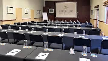 Uma sala de conferências com várias mesas, placas de identificação e uma tela exibindo 'HIPPO HOLLOW COUNTRY ESTATE'.