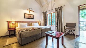 Quarto de hotel com cama, uma mesinha, uma cadeira e janela com cortinas.