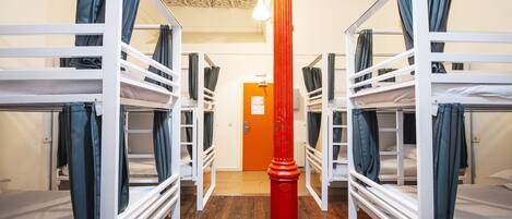 Quarto tipo dormitório com beliches, piso de madeira e um pilar central vermelho.