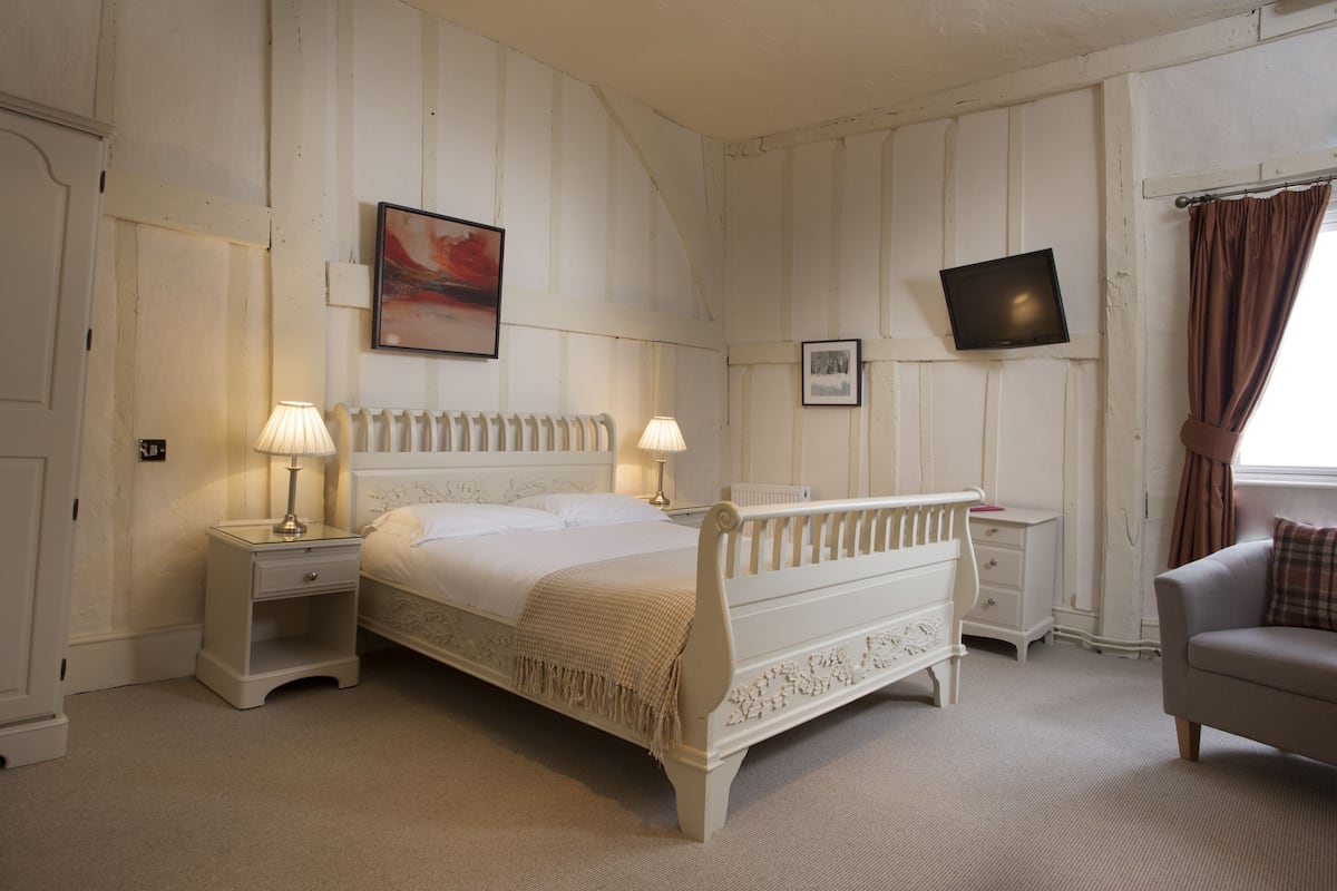 Quarto com cama, mesas de cabeceira, televisão e janela com cortinas.