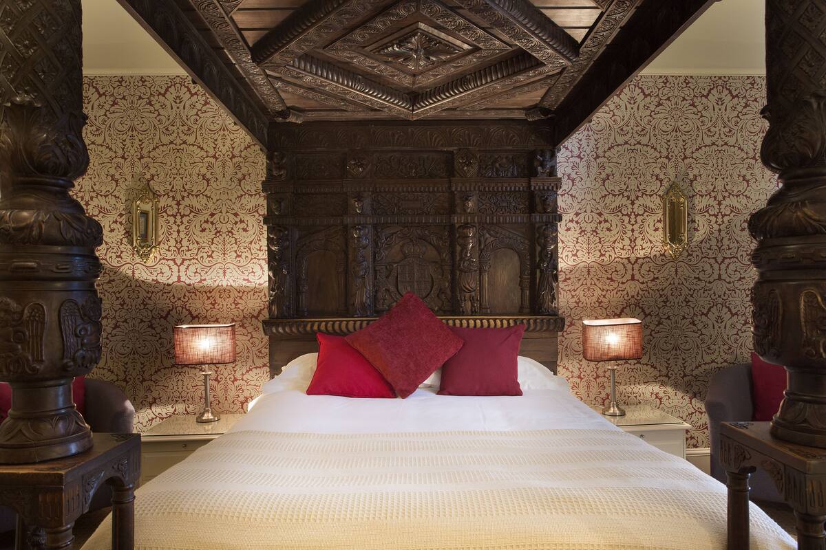 Quarto com cama grande, cabeceira de madeira ornamentada e duas luminárias de apoio.