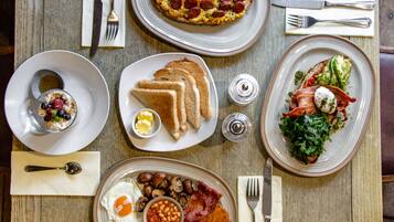 Uma mesa de café da manhã com pratos de ovos, torradas, feijão, bacon e outras opções para o café.