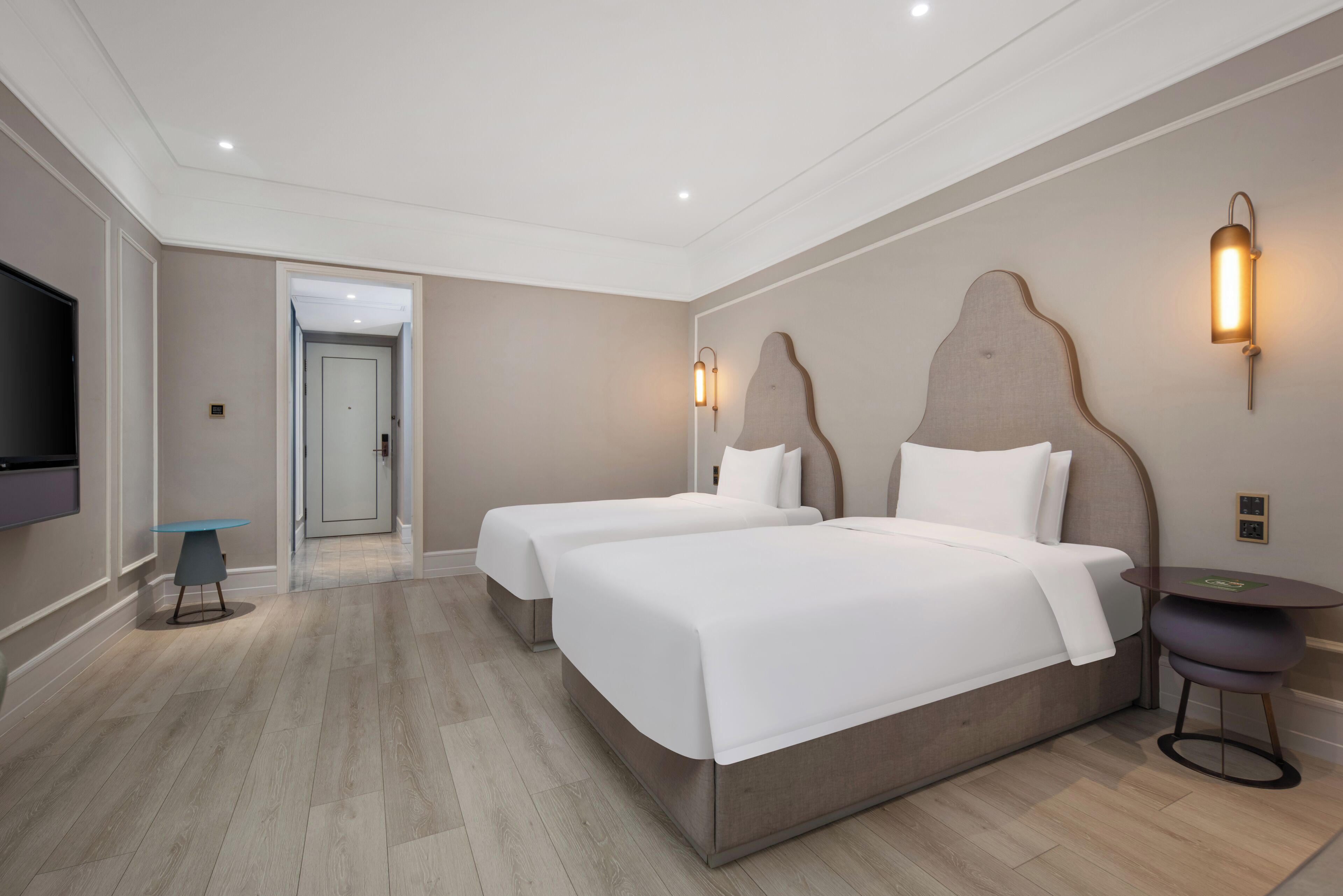 Quarto de hotel com duas camas, uma televisão de tela plana, uma mesinha e um candeeiro fixado na parede.