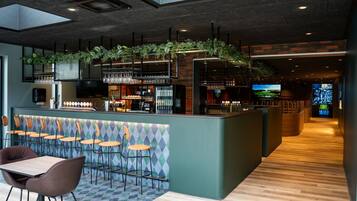 Uma área de bar moderna com balcão, banquetas e uma tela de televisão.