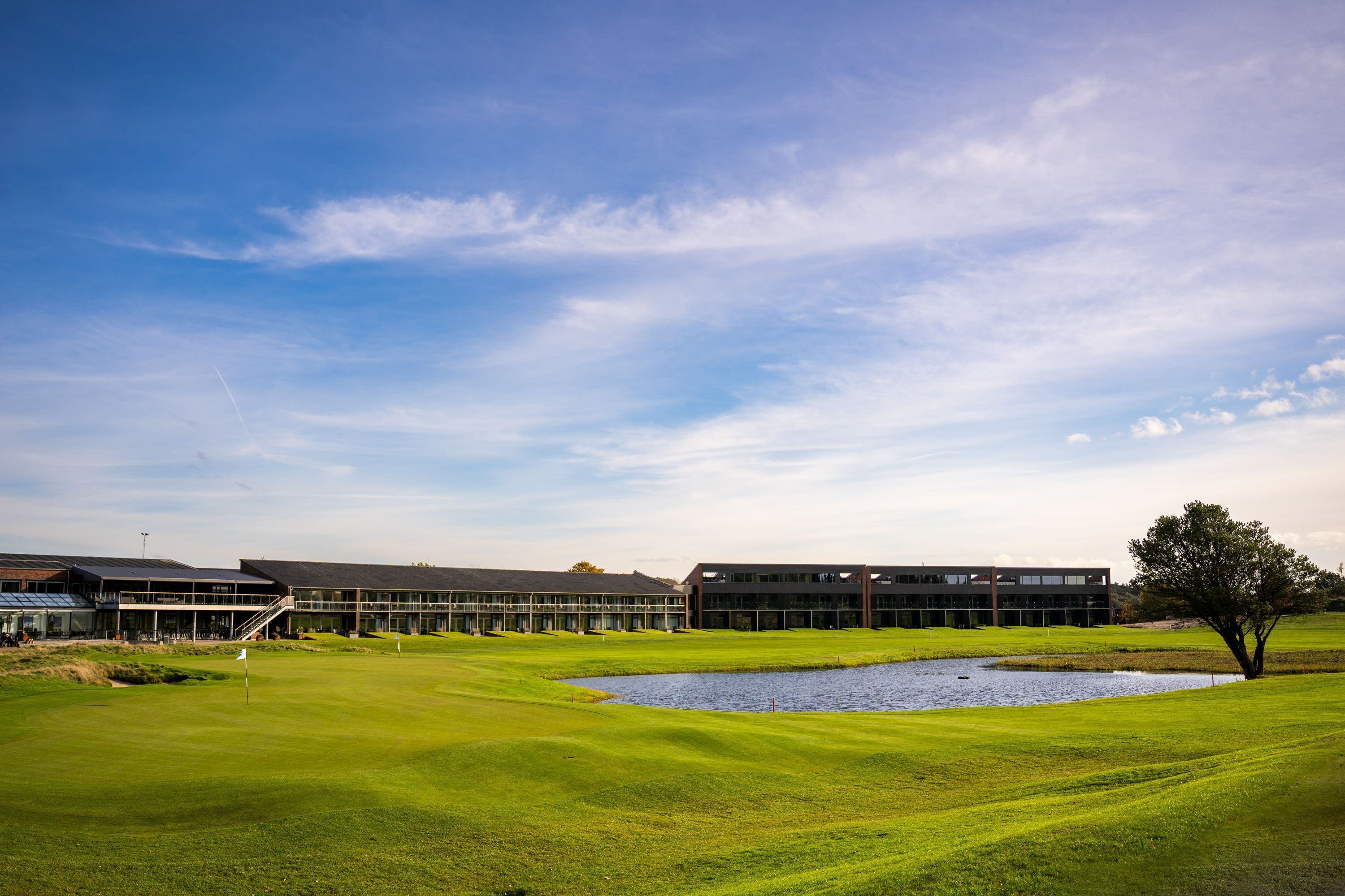 Um campo de golfe com um lago, um edifício com vários andares e uma árvore.