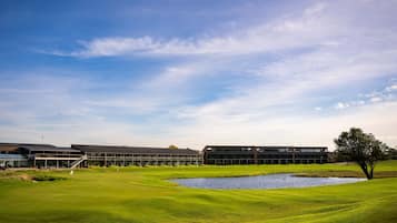 Um campo de golfe com um lago, um edifício com vários andares e uma árvore.
