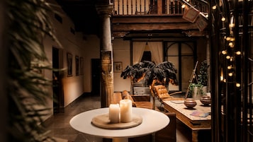 Um quarto com pouca luz, uma mesa redonda, uma poltrona de couro e uma planta decorativa.