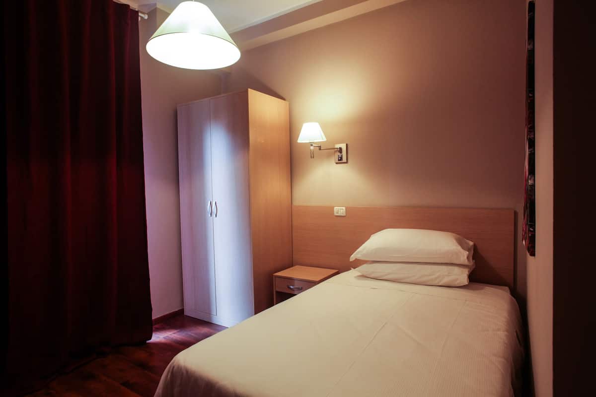 Quarto de hotel com cama, mesa de cabeceira, abajur, guarda-roupa e cortina.