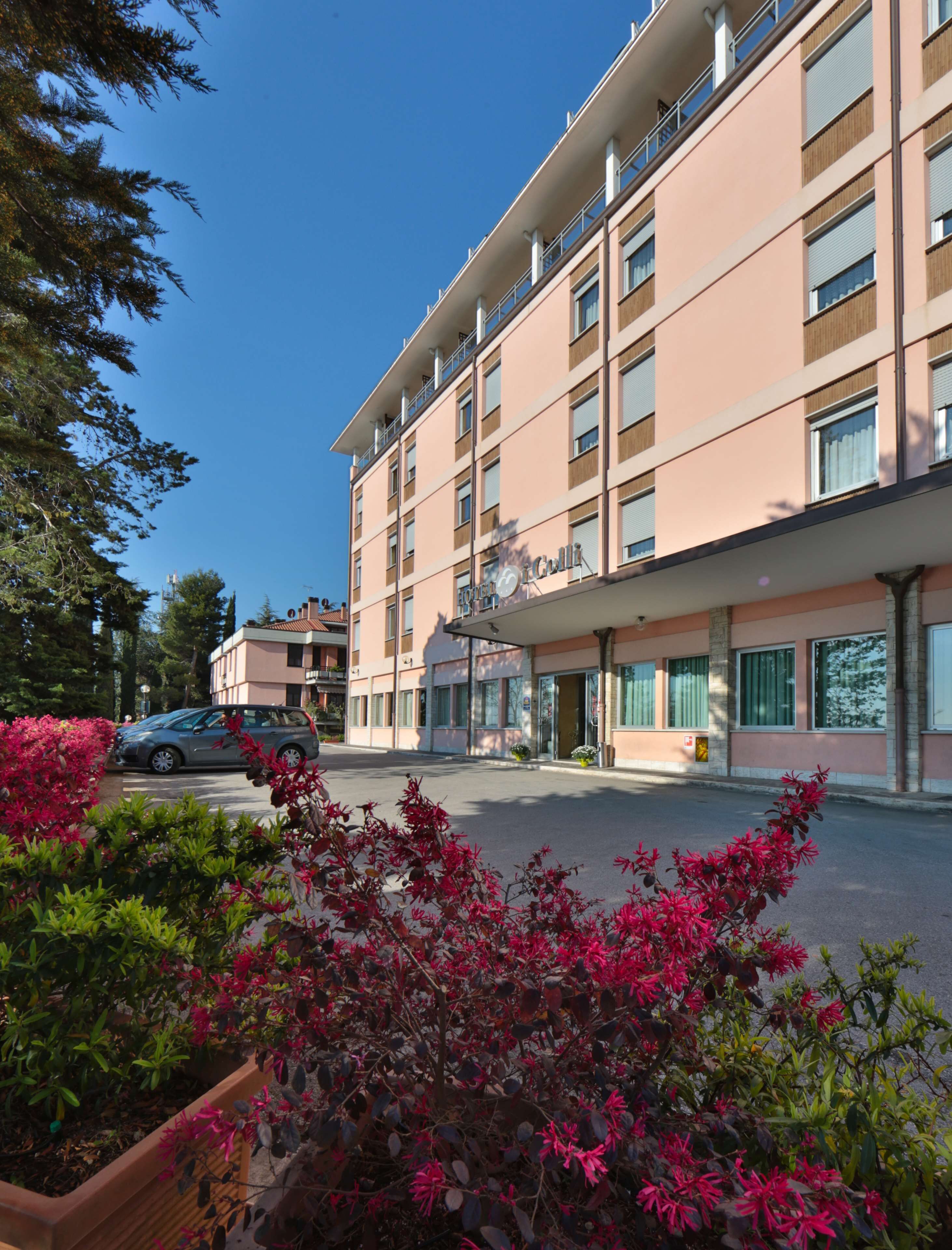 Hotel de vários andares com design moderno, destacando uma entrada imponente e uma área de estacionamento na frente.