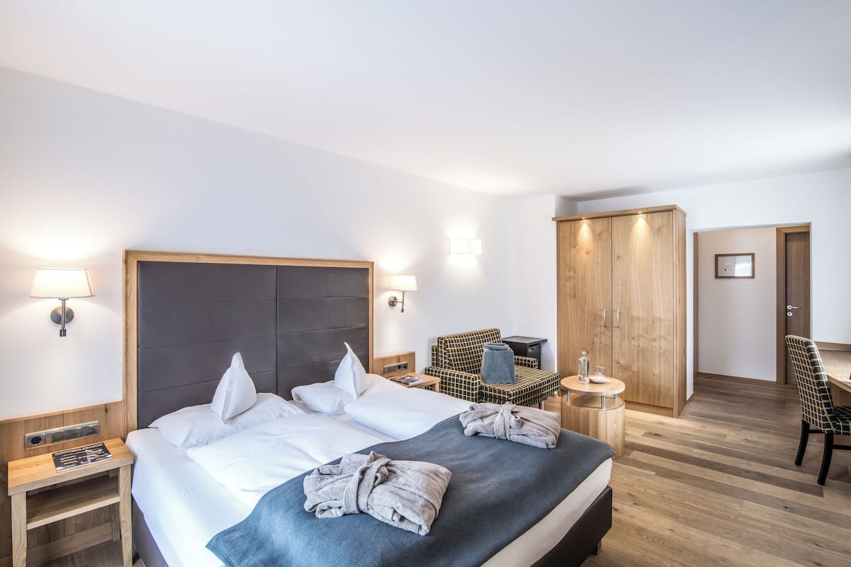 Quarto de hotel com cama grande, duas mesas de cabeceira, uma cadeira, escrivaninha e guarda-roupa.