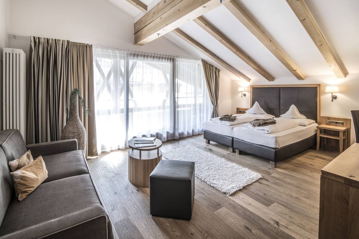 Quarto moderno com uma cama grande, um sofá, uma pequena mesa redonda e piso de madeira.