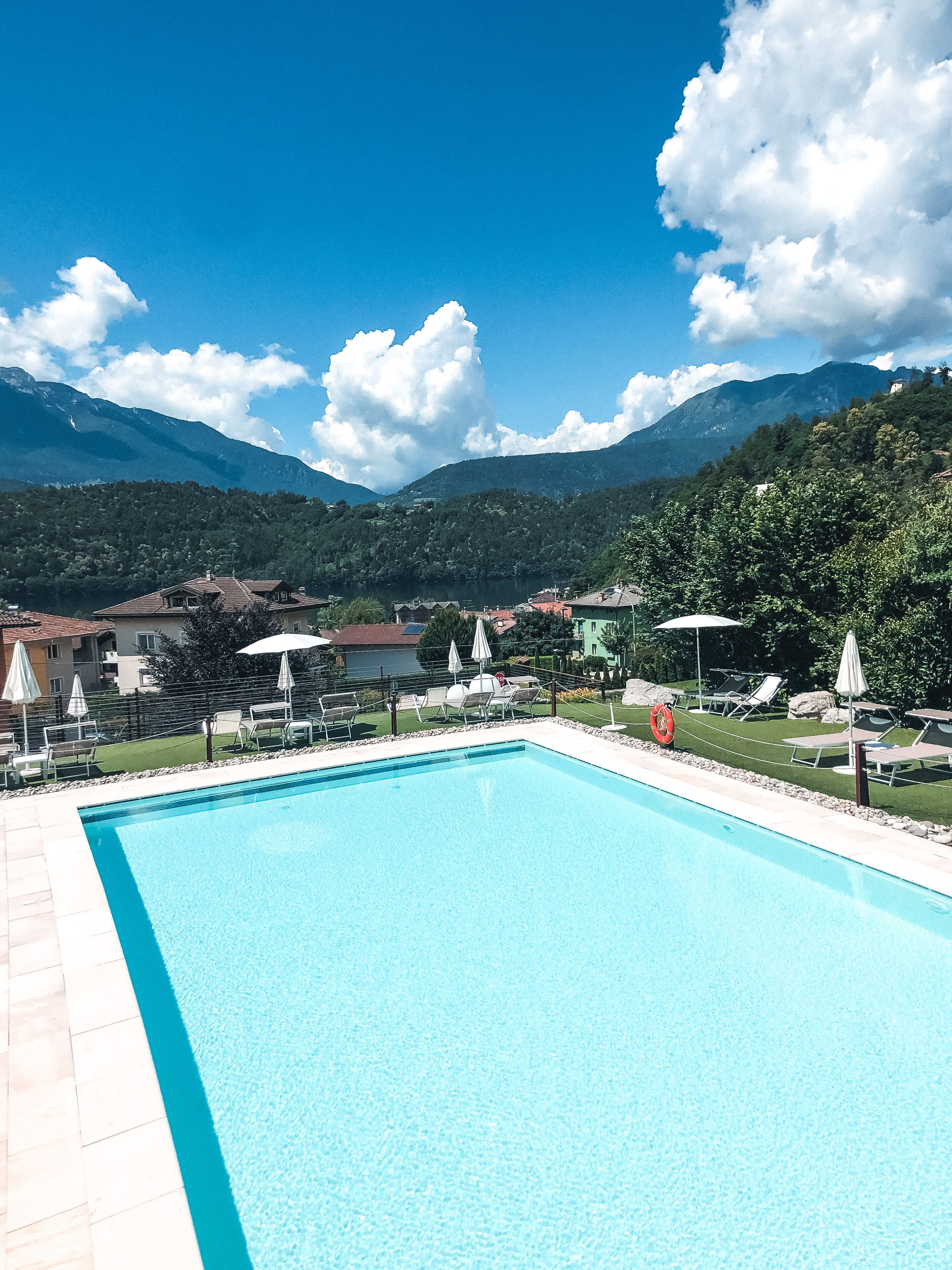Piscina com espreguiçadeiras e guarda-sóis, cercada por montanhas e vegetação.